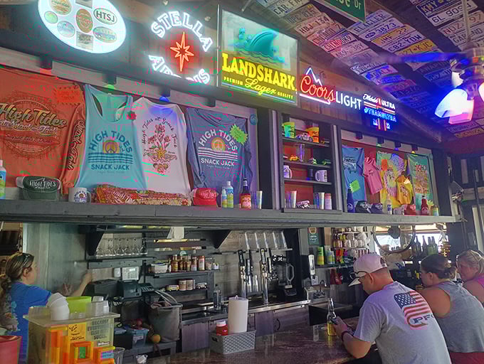The bar area—where neon signs, colorful t-shirts, and cold drinks create the perfect backdrop for stories that get better with each telling.