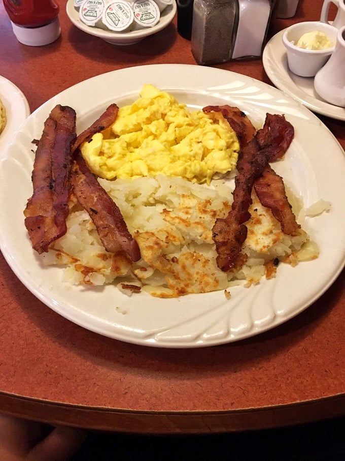 The breakfast trinity – eggs, bacon, and hash browns – performing their morning miracle with the synchronicity of a veteran jazz trio.