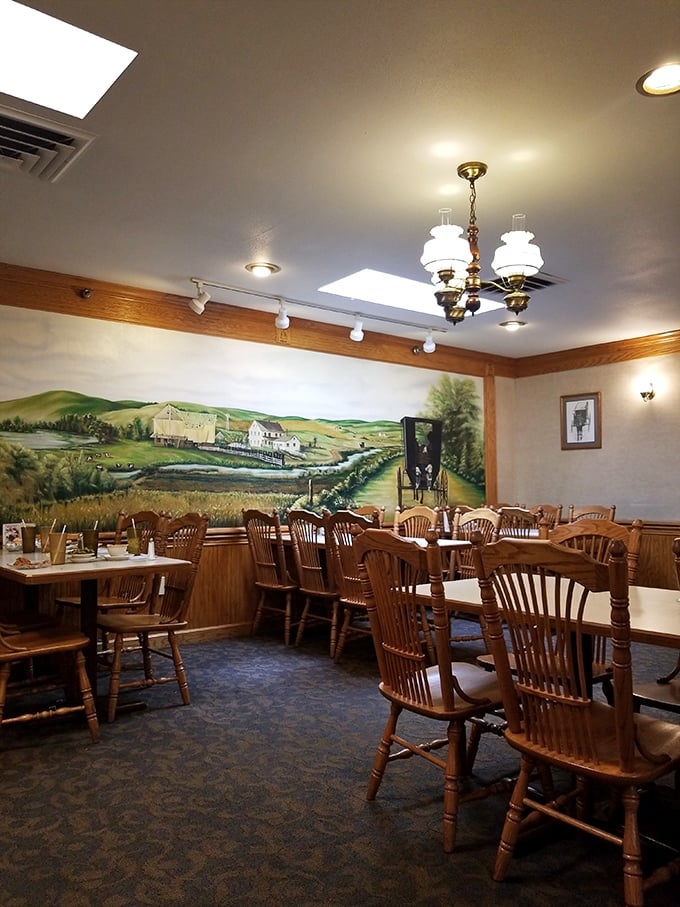 Rustic wooden chairs face a pastoral mural that serves as a window to simpler times—dining with a side of nostalgia.