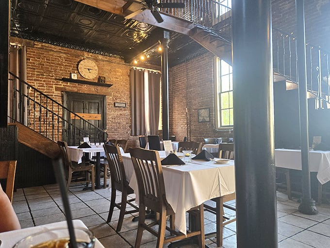 Tables spaced for privacy but close enough for community—where white tablecloths meet rustic brick in a dance of refined comfort.