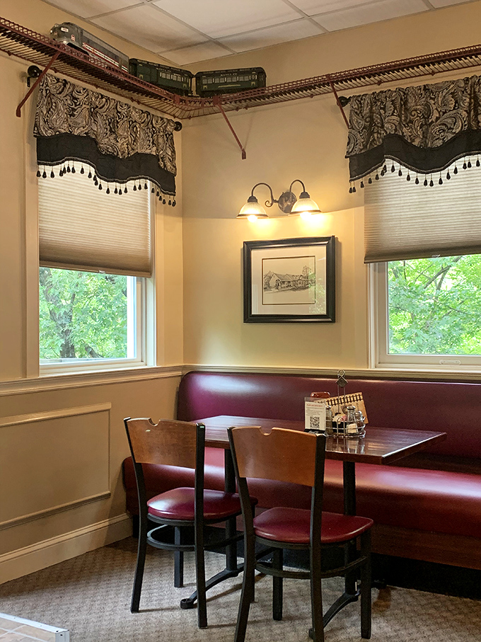 A model train circles above this cozy corner booth, where elegant window treatments frame views of greenery outside—transportation themes that go beyond decoration.