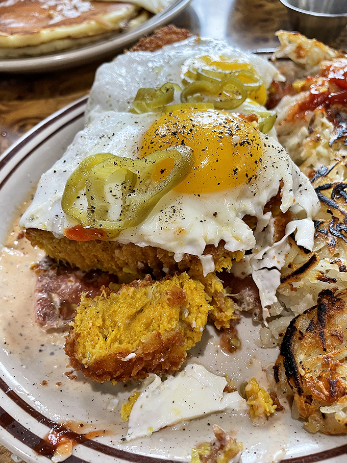 A sunny-side up egg perched atop what appears to be cornbread and scrapple—proof that breakfast architecture should be taught in design schools.