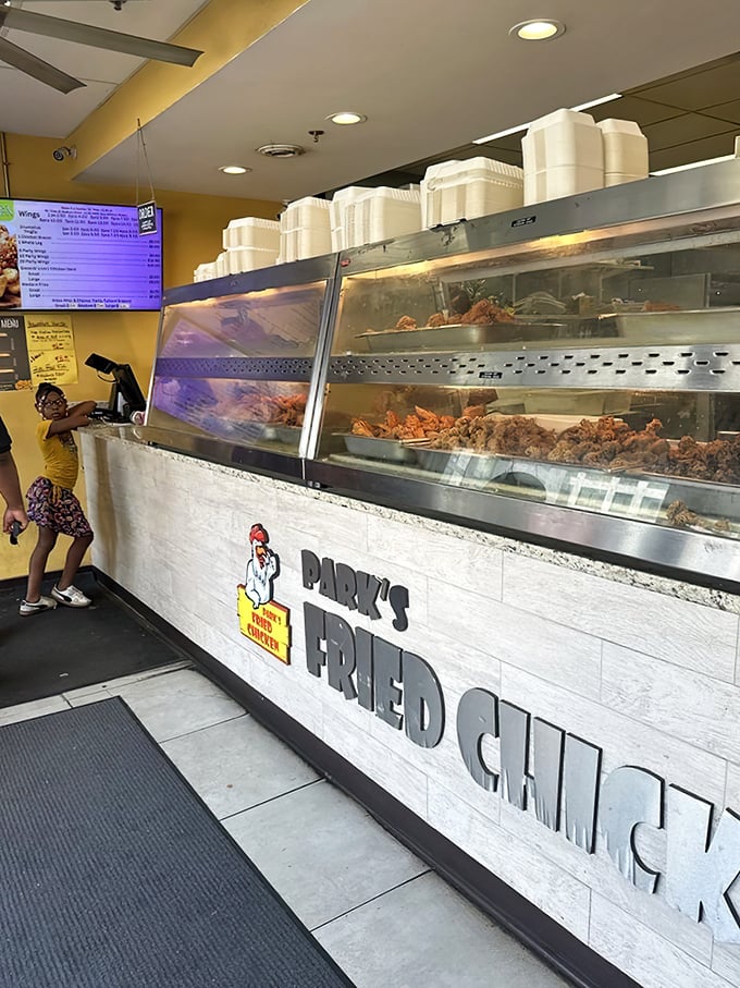 Behind this counter, culinary magic happens daily. The display case showcases treasures more valuable than gold to fried chicken aficionados.