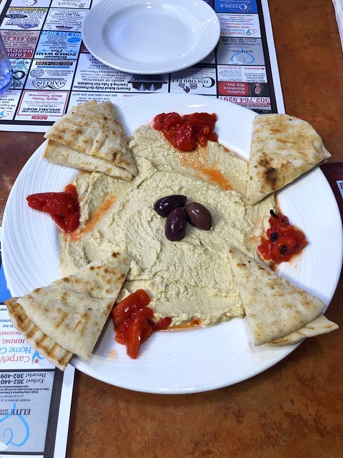 Hummus that doesn't just sit on the plate—it lounges luxuriously, surrounded by its entourage of warm pita, roasted peppers, and plump olives.