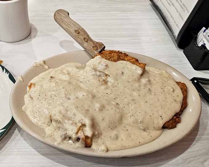 Country fried steak swimming in gravy—where the knife stands at attention in the middle like it's claiming this delicious territory for comfort food nation.