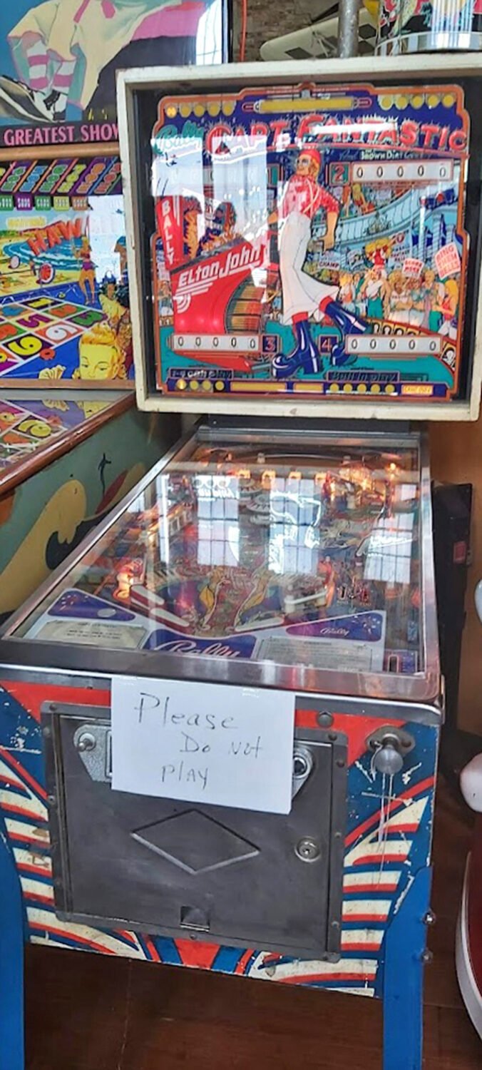 Vintage pinball machines with their "Please Do Not Play" signs—the ultimate temptation for fingers that remember the thrill of the flippers.