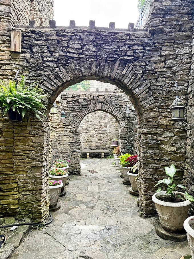 Stone archways frame garden pathways where potted plants add life and color. Medieval aesthetics meet modern gardening in this tranquil courtyard space.