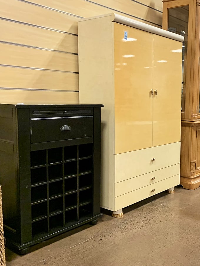 A mid-century wine rack and cream wardrobe stand side by side—furniture from different eras finding common ground in thrift store harmony.