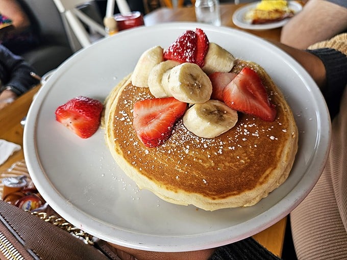 These pancakes don't just arrive at your table—they make an entrance, dressed in their finest fruit finery and powdered sugar snowfall. 