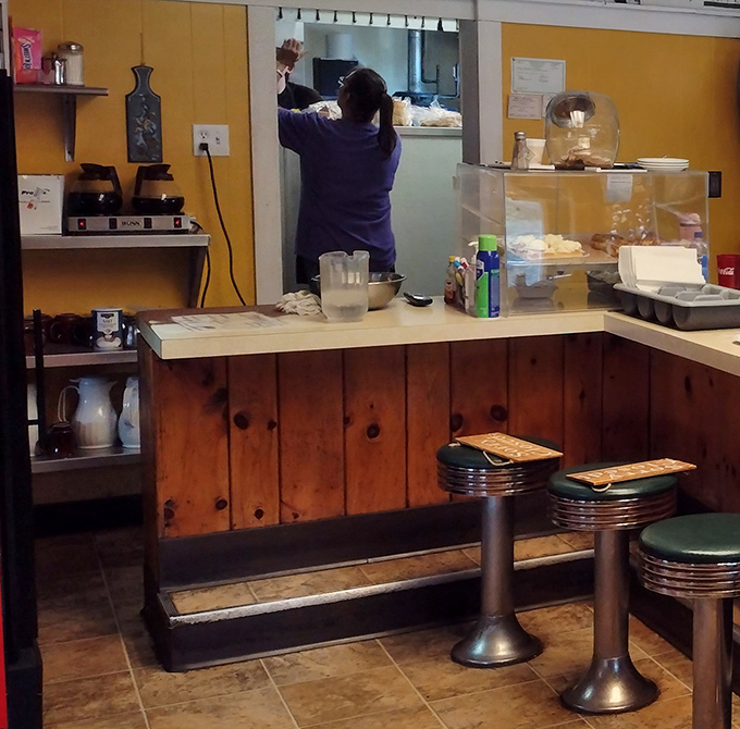 Where breakfast magic happens—the kitchen pass offering a glimpse into the choreography of comfort food creation.