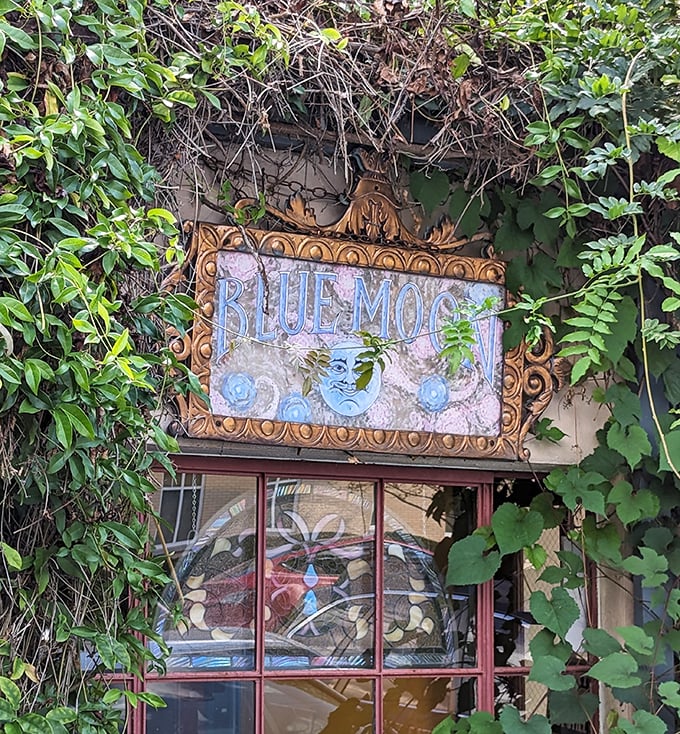 The Blue Moon Café's whimsical sign peeks through a curtain of greenery, like a secret garden that happens to serve incredible food.