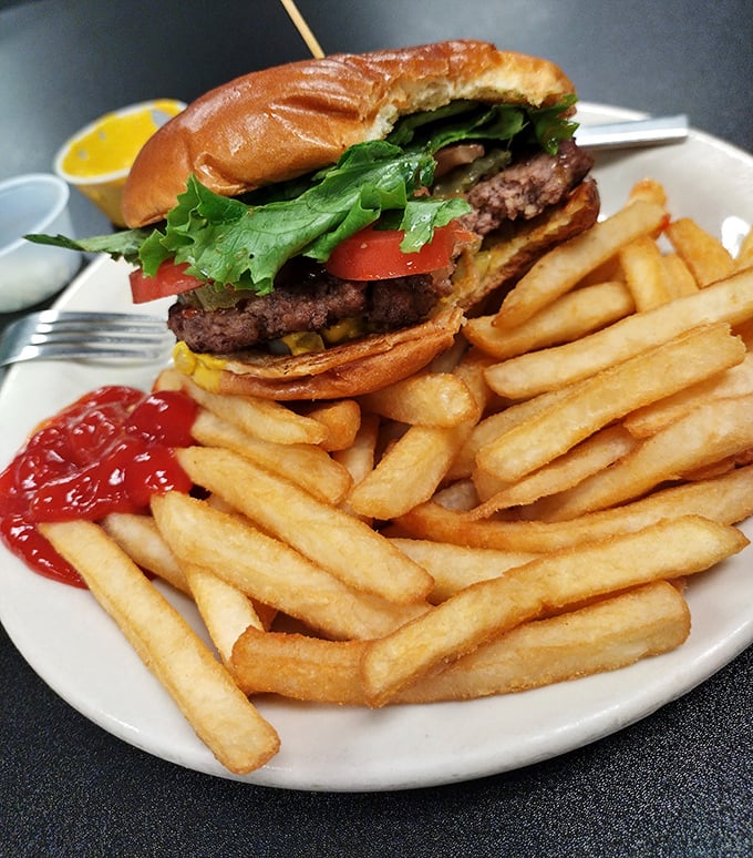 A burger that requires two hands and a strategy, accompanied by a golden army of crispy fries—simple food executed with the confidence of experience.