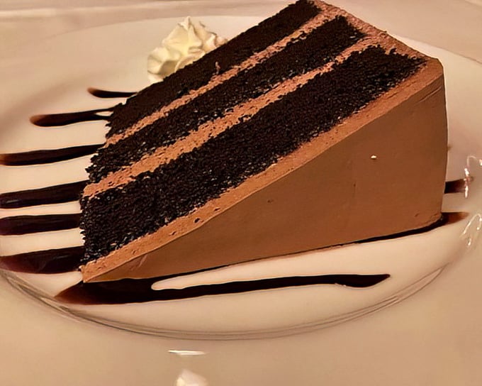 A slice of chocolate cake so imposing it deserves its own zip code – layers of dark decadence separated by creamy frosting.