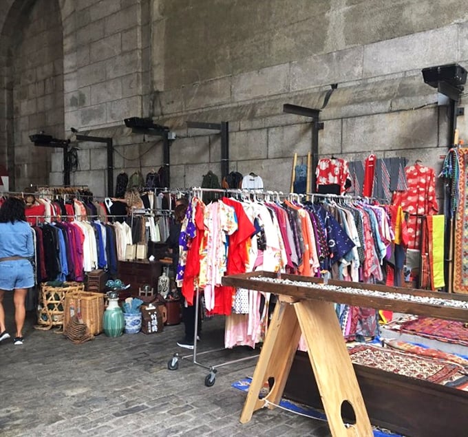 Vintage clothing racks beneath stone arches create a cathedral of style. Yesterday's fashion finds tomorrow's devotees in this sacred space.
