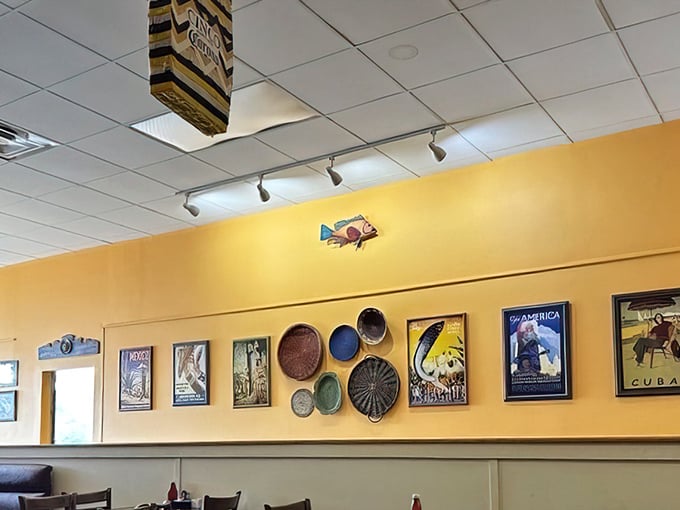 The wall art collection tells stories without saying a word. Those vintage travel posters and colorful plates transform a simple yellow wall into a conversation starter.