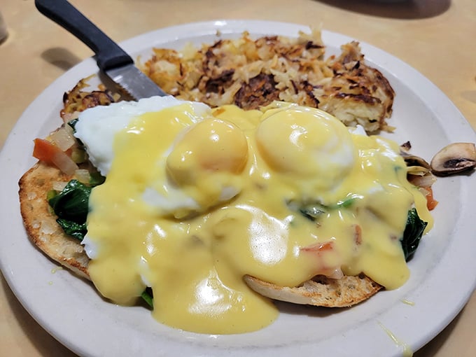 Hollandaise cascading over poached eggs like yellow velvet—this Benedict isn't just breakfast, it's performance art with hash browns as the supporting cast.