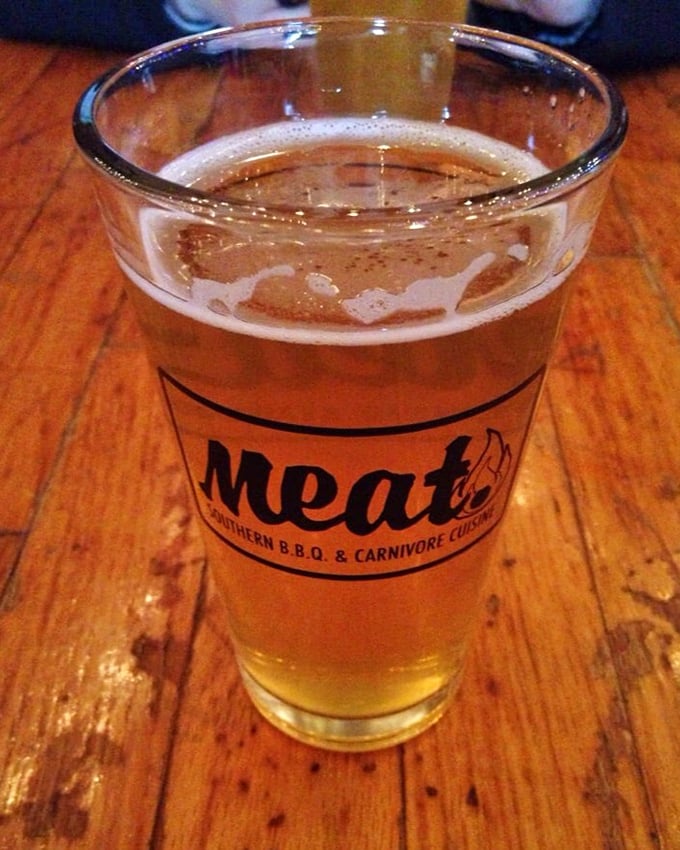A golden glass of beer bearing the Meat BBQ logo—because what pairs better with smoked meats than a cold, crisp brew?