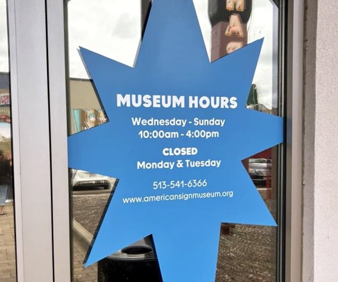 The museum hours sign shaped like a starburst—because when you're in the sign business, even your schedule deserves flair.