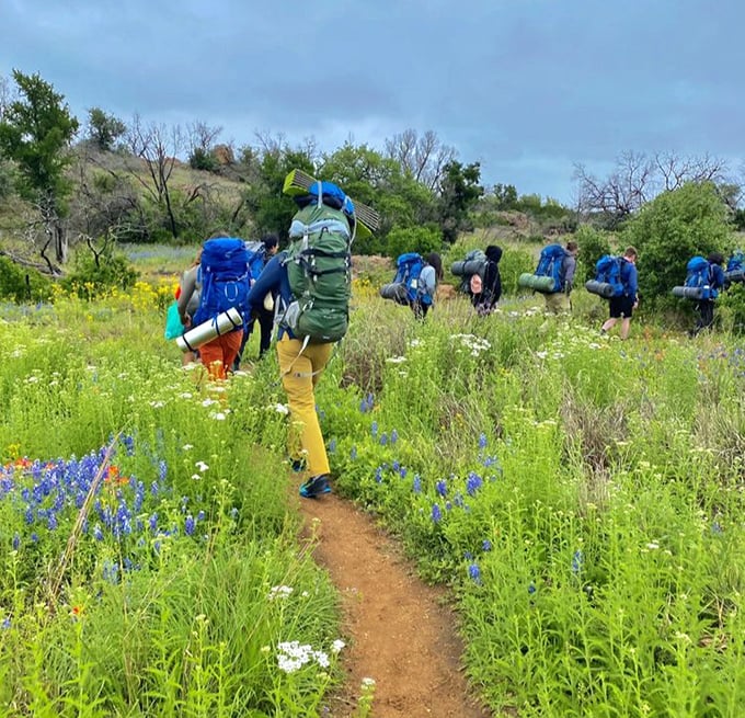 Backpackers traverse wildflower meadows, looking like a walking REI commercial but with better scenery.