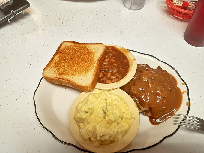 A humble plate of comfort featuring toast, potato salad, beans, and gravy-smothered meat—the kind of meal that makes you understand why diners endure.