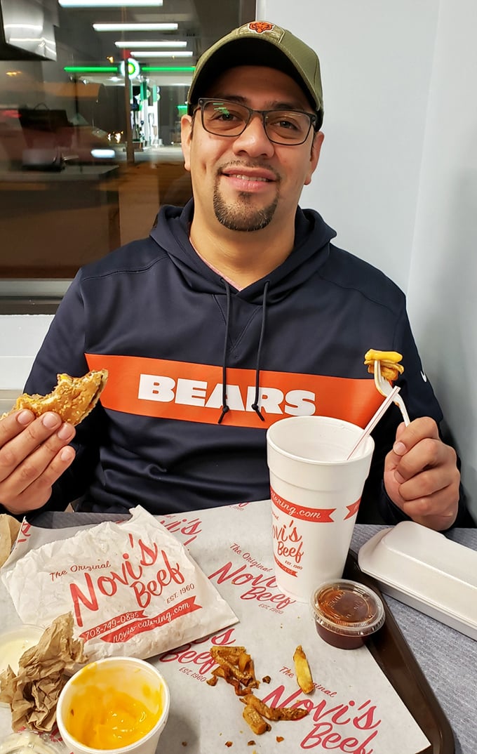 A satisfied customer shows off his Novi's feast, sporting Chicago Bears gear—because local loyalty extends from stadium to sandwich shop.