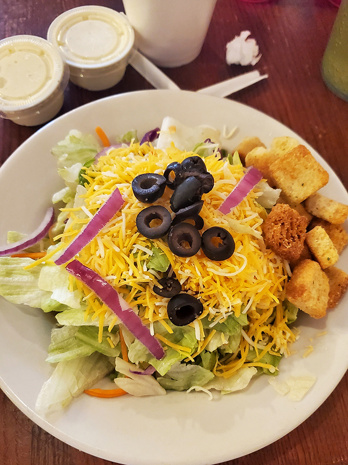 A salad that doesn't apologize for its simplicity—crisp lettuce, generous cheese, and those perfectly sliced olives arranged like they're posing for their yearbook photo.