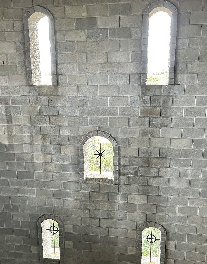 Medieval minimalism at its finest—simple stone walls punctuated by arched windows with cross designs create a contemplative atmosphere.