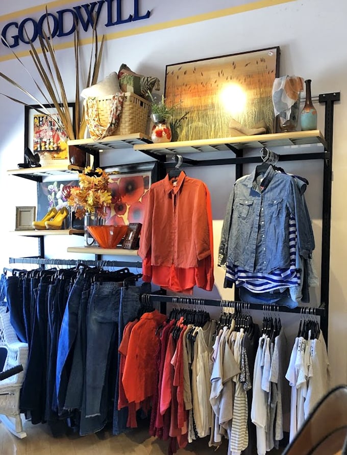 A fashion treasure trove awaits! Neatly organized racks showcase denim, bright orange blouses, and striped shirts—proof that sustainable style doesn't require a second mortgage.