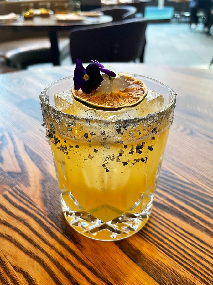 This isn't just a cocktail—it's liquid sunshine with salt rim, dried citrus, and an edible flower that makes happy hour truly happy.