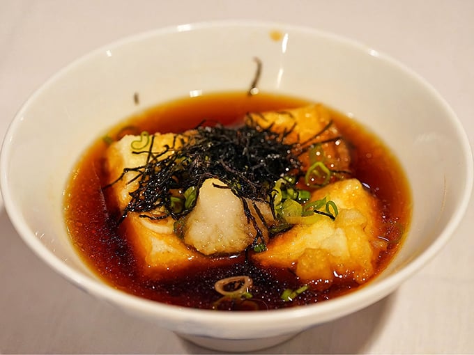 Agedashi tofu swimming in delicate dashi broth—crispy exterior giving way to silken interior, topped with bonito flakes dancing in the steam.