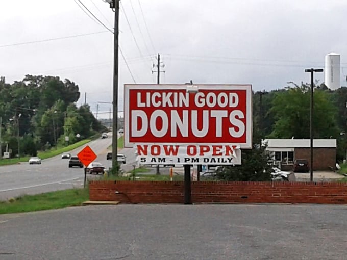 The roadside sign announces operating hours of 5 AM to 1 PM daily—a gentle reminder that the early bird gets the still-warm donut.