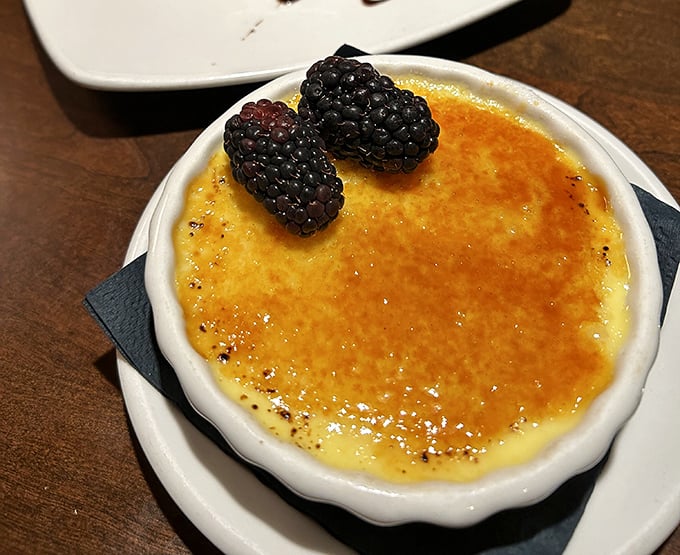 The crème brûlée's perfectly torched sugar crust awaits your spoon's satisfying crack, topped with plump blackberries for a touch of tartness.