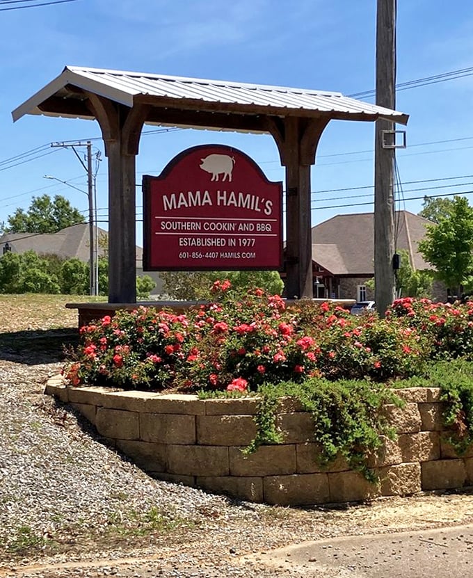 The sign stands like a beacon of hope for hungry travelers—surrounded by roses as if nature itself is celebrating what awaits inside.