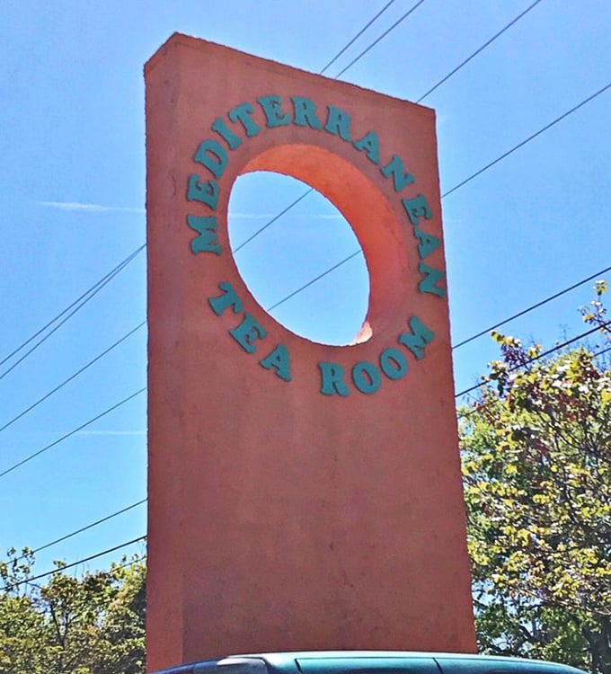 The sign stands as a beacon for those in the know. Orange against blue sky—Mediterranean colors signaling authentic flavors await.