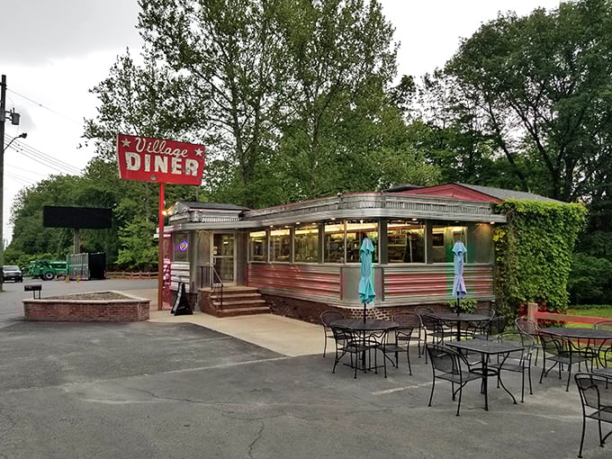 The Village Diner's classic stainless steel exterior gleams in the sunlight, a shiny time capsule with red stripes and turquoise umbrellas inviting you to step back in time.