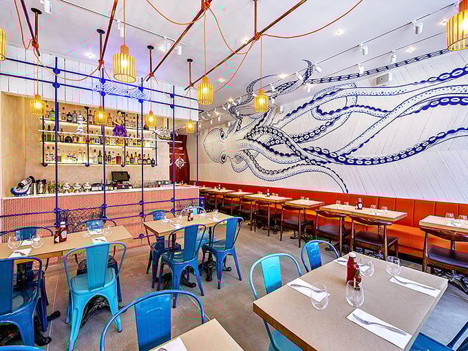 Inside, an octopus mural watches over diners while blue metal chairs and warm pendant lighting create the perfect balance of nautical charm and urban cool.