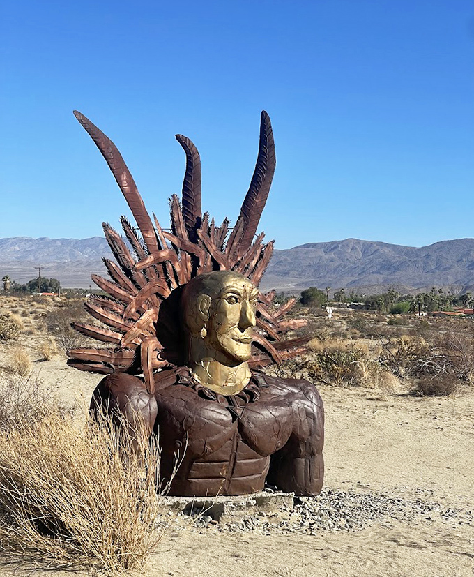 This majestic Native American warrior bust, complete with golden face and impressive headdress, stands sentinel over the desert landscape.