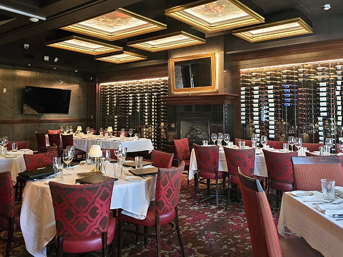 Wine bottles line the walls like silent sentinels guarding flavor treasures, while rich burgundy chairs invite you to settle in for a memorable feast.