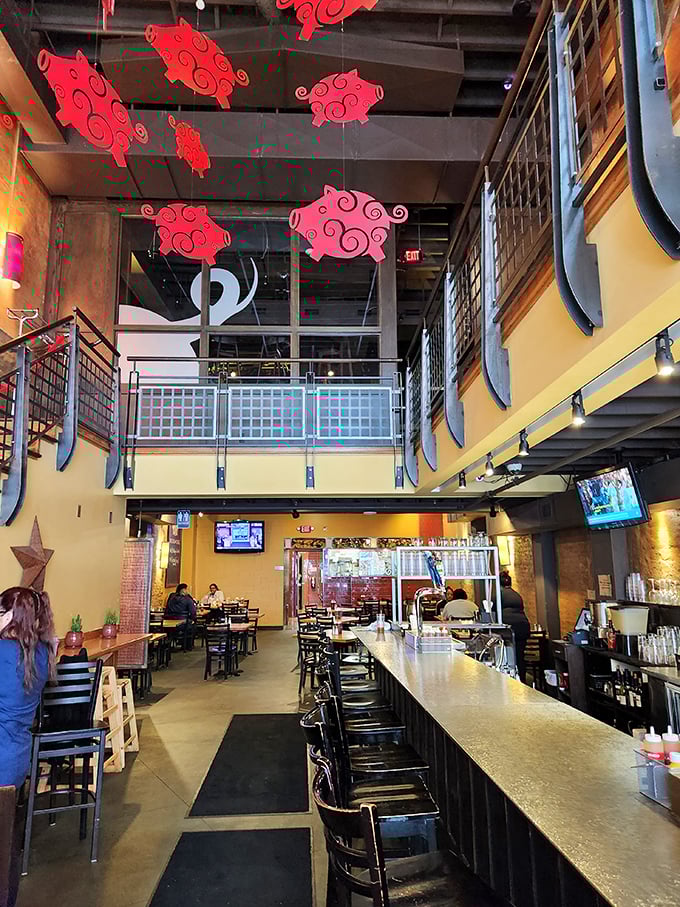 Whimsical red pig cutouts dance overhead in the two-story space where industrial chic meets Southern comfort – a perfect urban setting for BBQ indulgence.