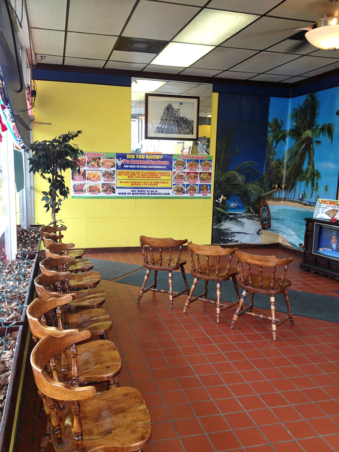 Wooden chairs and tropical murals create a humble oasis. The Caribbean beach scene promises an escape, but the chicken delivers the real vacation.