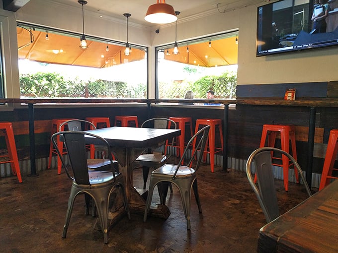 Industrial-chic meets comfort in this thoughtfully designed space where bright orange stools pop against metal chairs and wooden tables—perfect for serious hot dog contemplation.