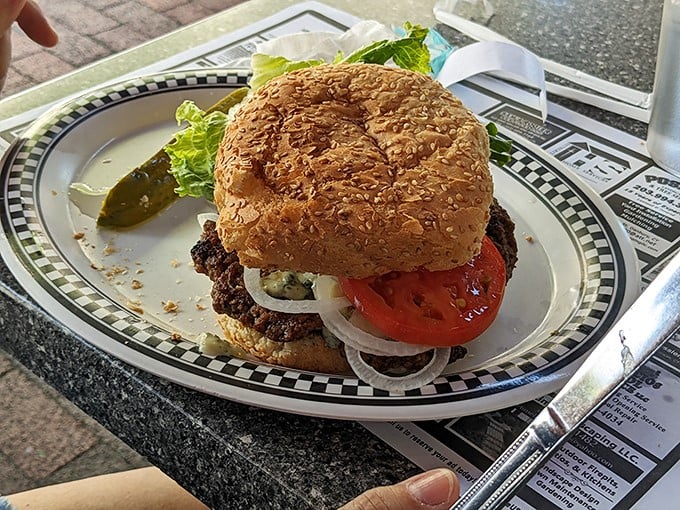 Behold the star of the show—a perfectly grilled burger on a sesame seed bun. That pickle on the side isn't just garnish, it's essential balance.