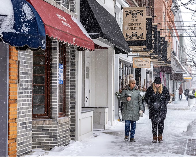 Two friends brave a snowfall on Second Avenue, coffee in hand. In Alpena, winter isn't endured—it's embraced with good company.