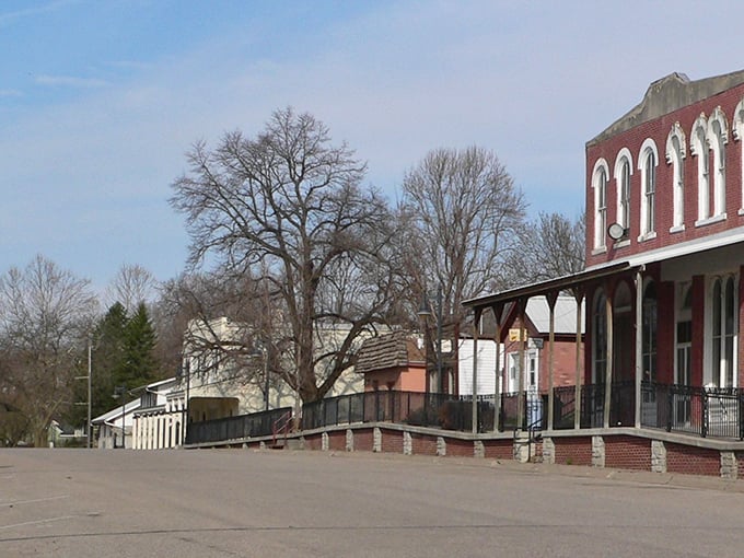 Victorian buildings with ornate arched windows overlook a peaceful town square framed by leafless trees.