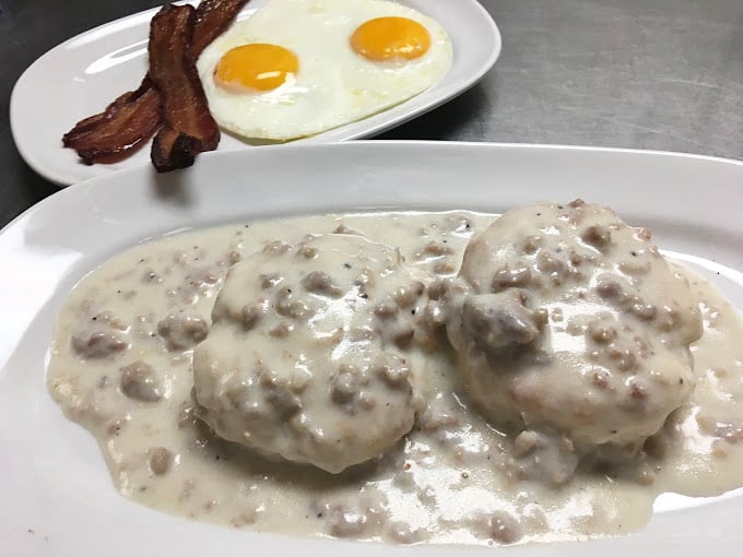 Behold the crown jewel: biscuits swimming in peppery sausage gravy alongside perfectly fried eggs and bacon – a breakfast trinity that inspires religious devotion.