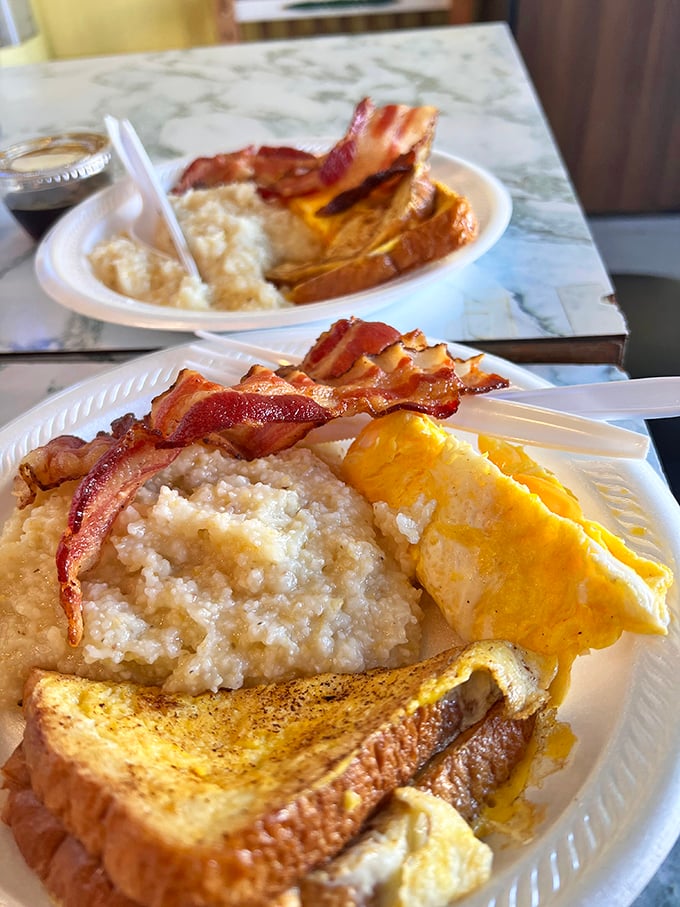 Breakfast nirvana: creamy grits, perfectly folded eggs, crispy bacon, and golden toast – the four food groups of Southern morning happiness on a single plate.