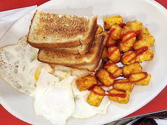 Breakfast perfection on a plate: golden toast, perfectly cooked eggs, and those tater tots with a drizzle of ketchup—proof that sometimes the simplest meals bring the greatest joy.