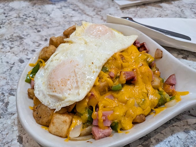 Breakfast architecture at its finest—crispy potatoes supporting a melty cheese roof, with ham and peppers playing structural support beneath sunny-side-up skylights.