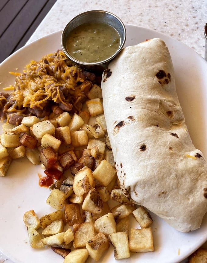 Behold the breakfast burrito in its natural habitat—surrounded by perfectly crisped potatoes and a side of green chile that means business.