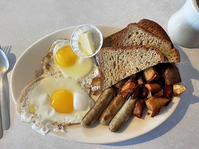 Two sunny-side-up eggs, perfectly browned home fries, and sausage links—the breakfast trinity that proves simplicity is the ultimate sophistication.